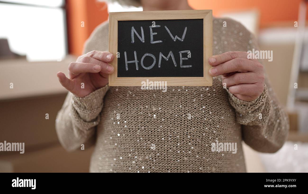 Middle age woman with grey hair holding blackboard standing at new home ...