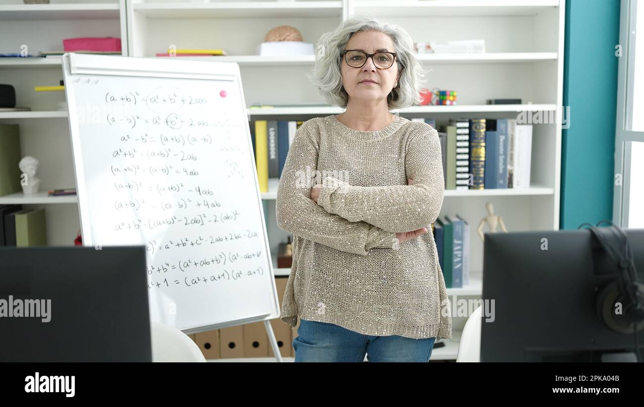 Middle age woman with grey hair teacher standing with arms crossed gesture at university ...