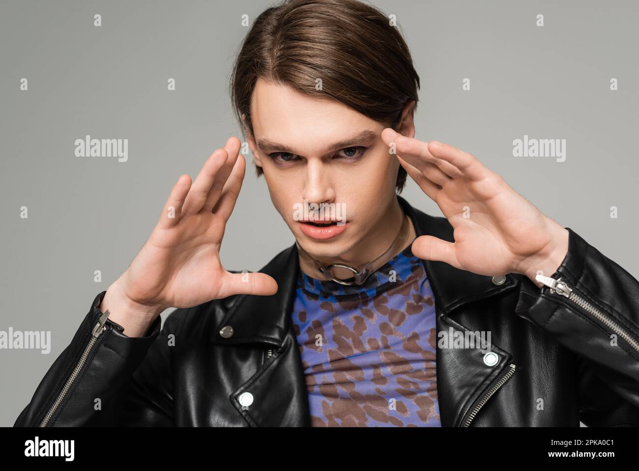 portrait of trendy bigender model in black leather jacket holding hands ...
