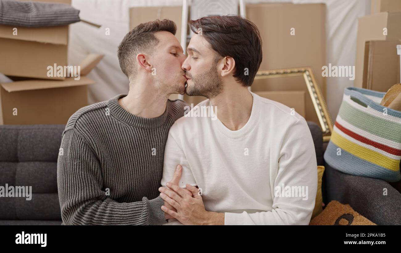 Two men couple sitting on sofa hugging each other kissing at new home Stock Photo - Alamy