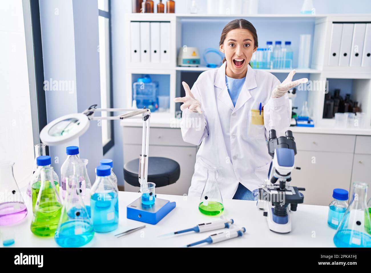 Young brunette woman working at scientist laboratory celebrating victory with happy smile and ...