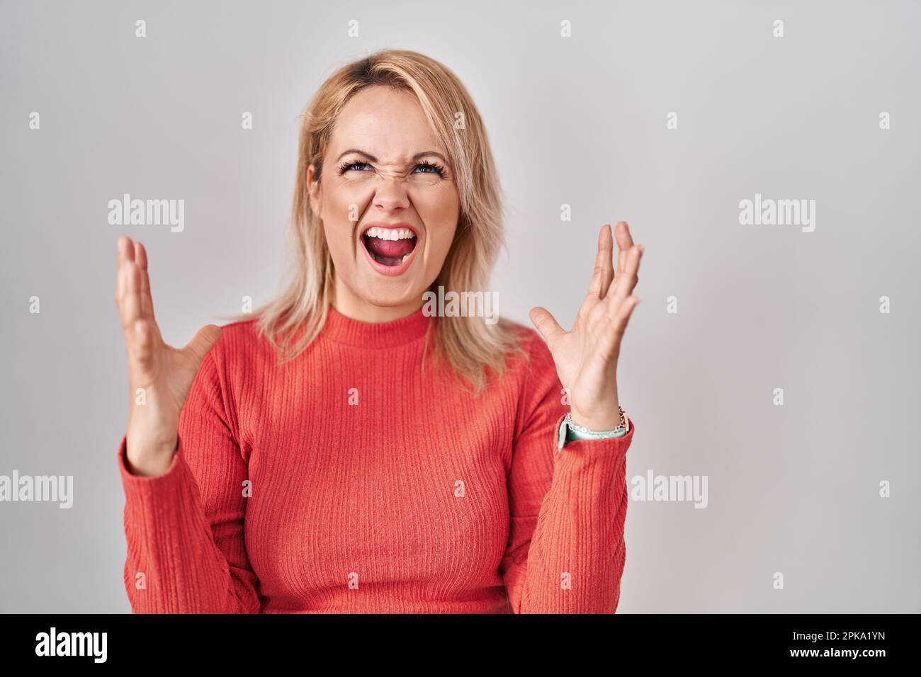 Blonde woman standing over isolated background crazy and mad shouting ...