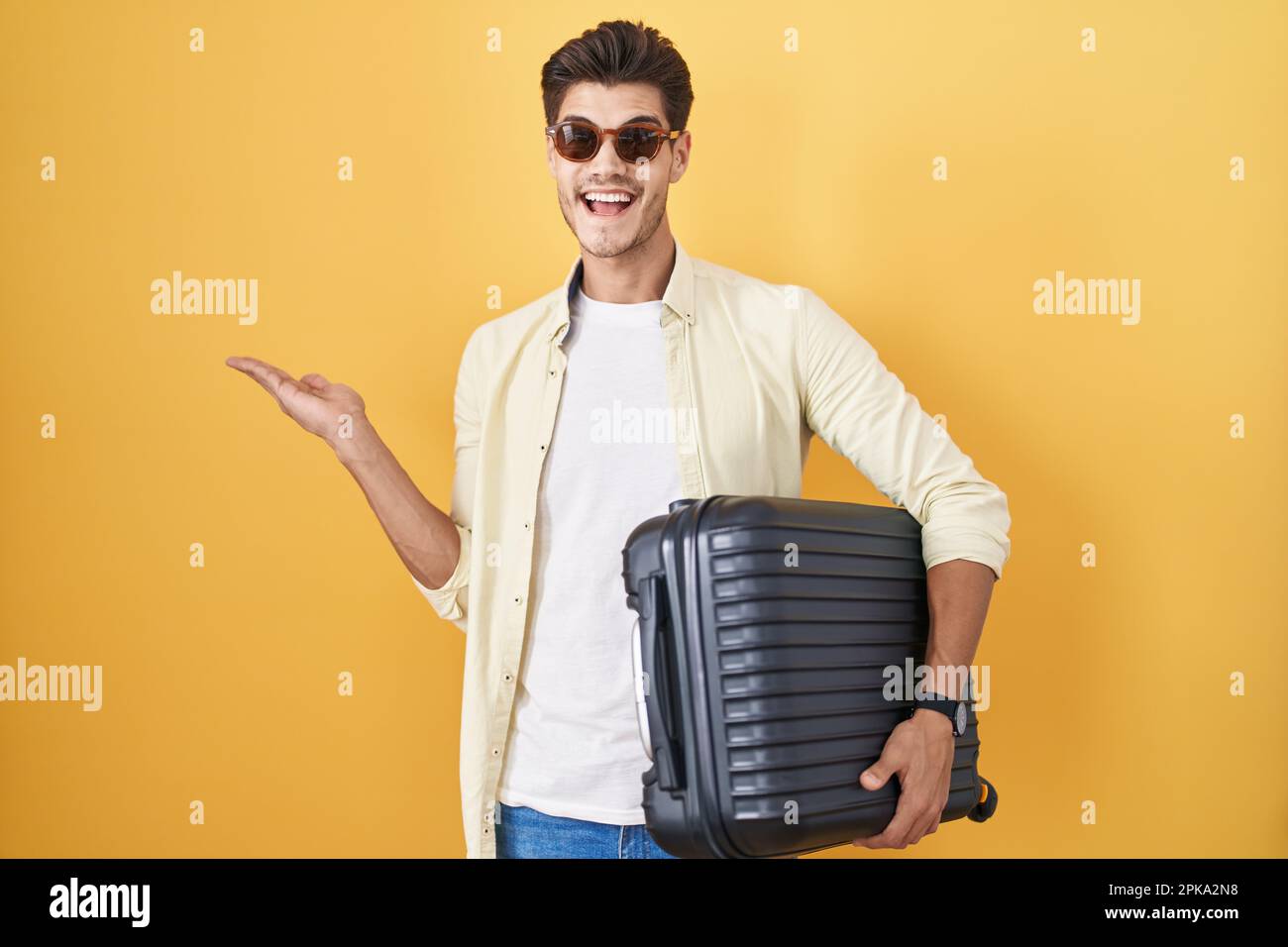Young hispanic man holding suitcase going on summer vacation pointing ...