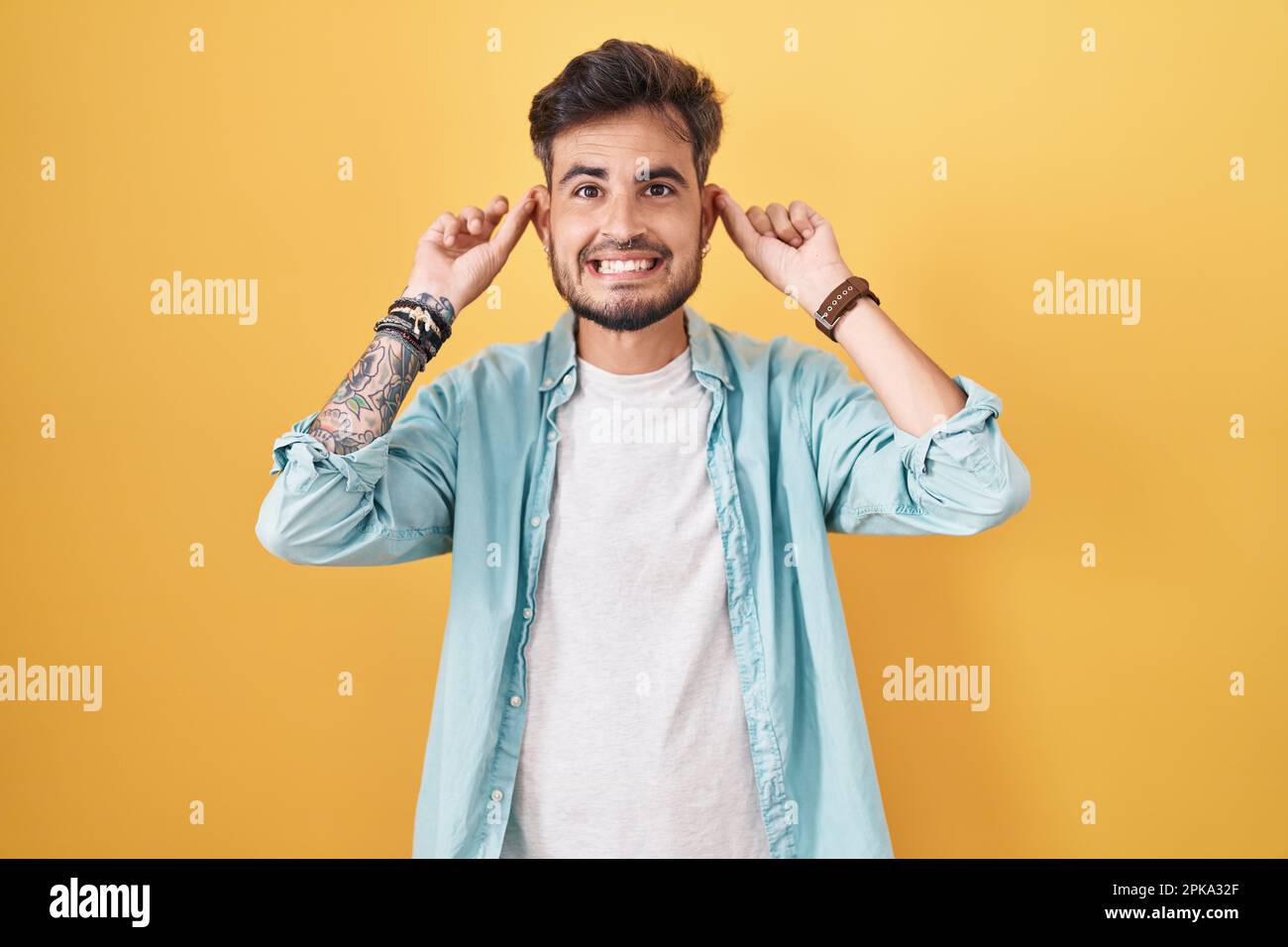 Young hispanic man with tattoos standing over yellow background smiling ...