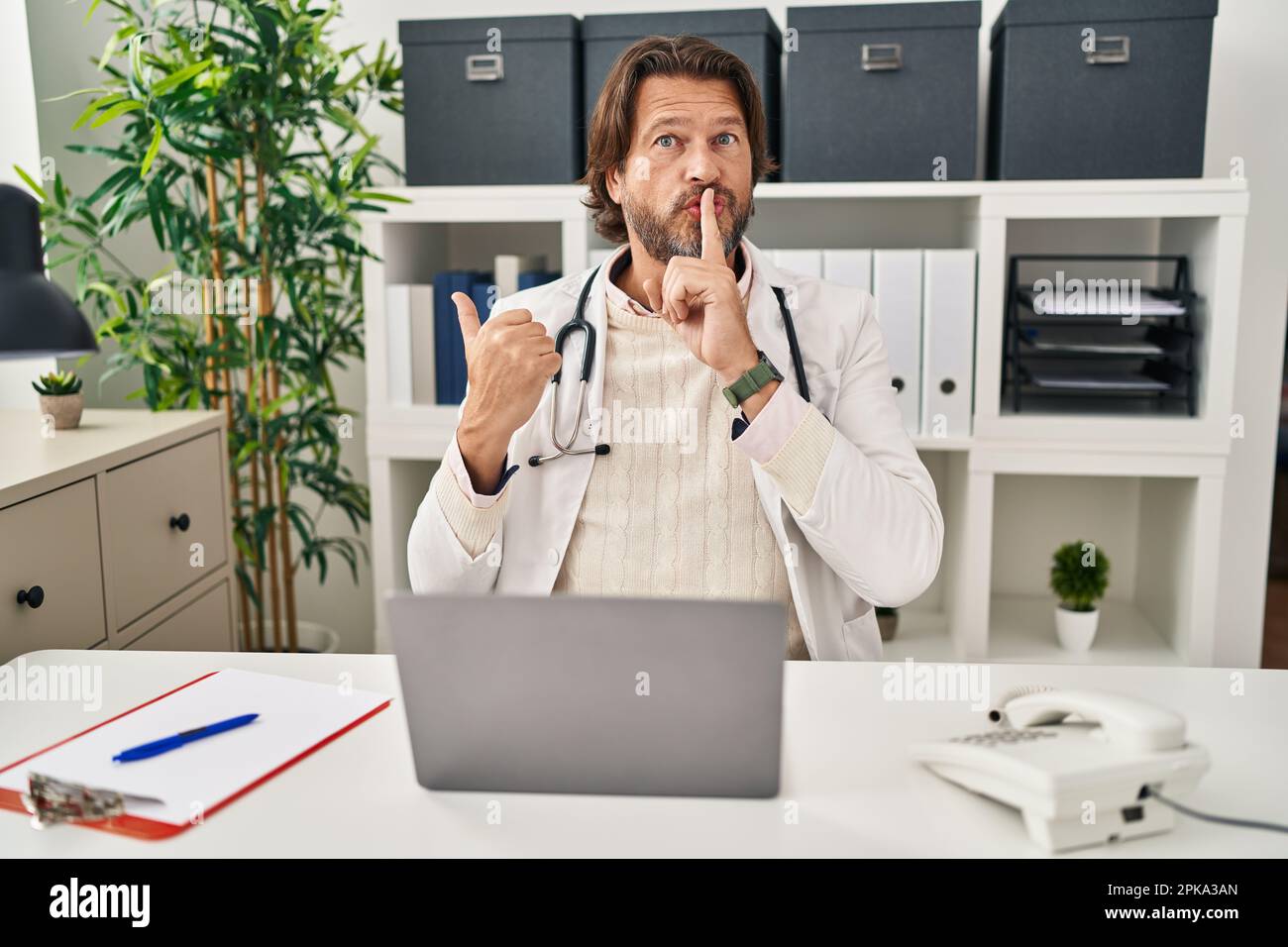Handsome middle age doctor man working at the clinic asking to be quiet ...