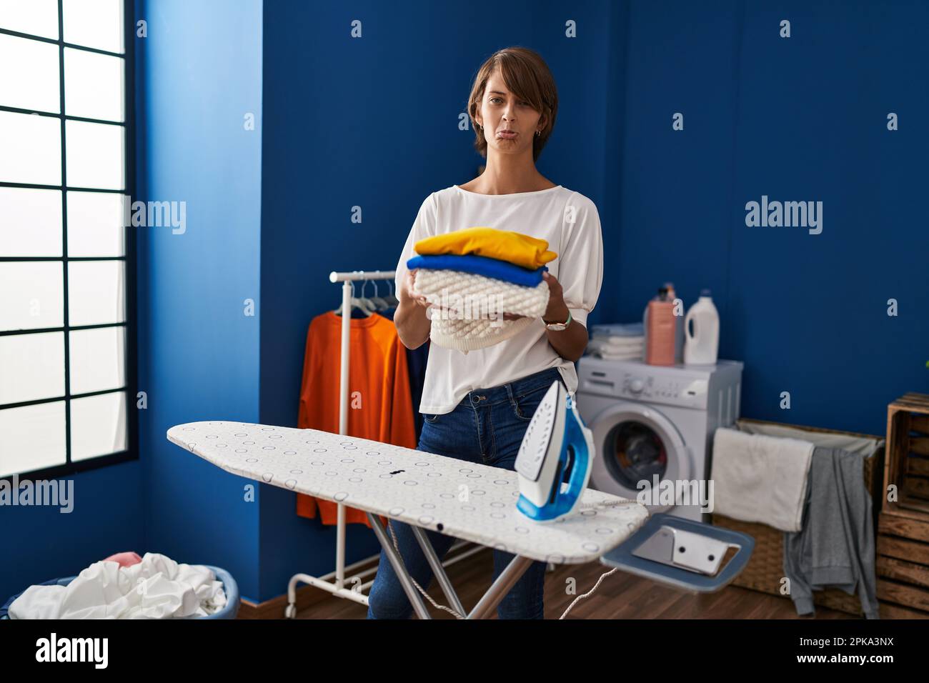 Brunette woman holding folded laundry after ironing depressed and worry for distress, crying ...