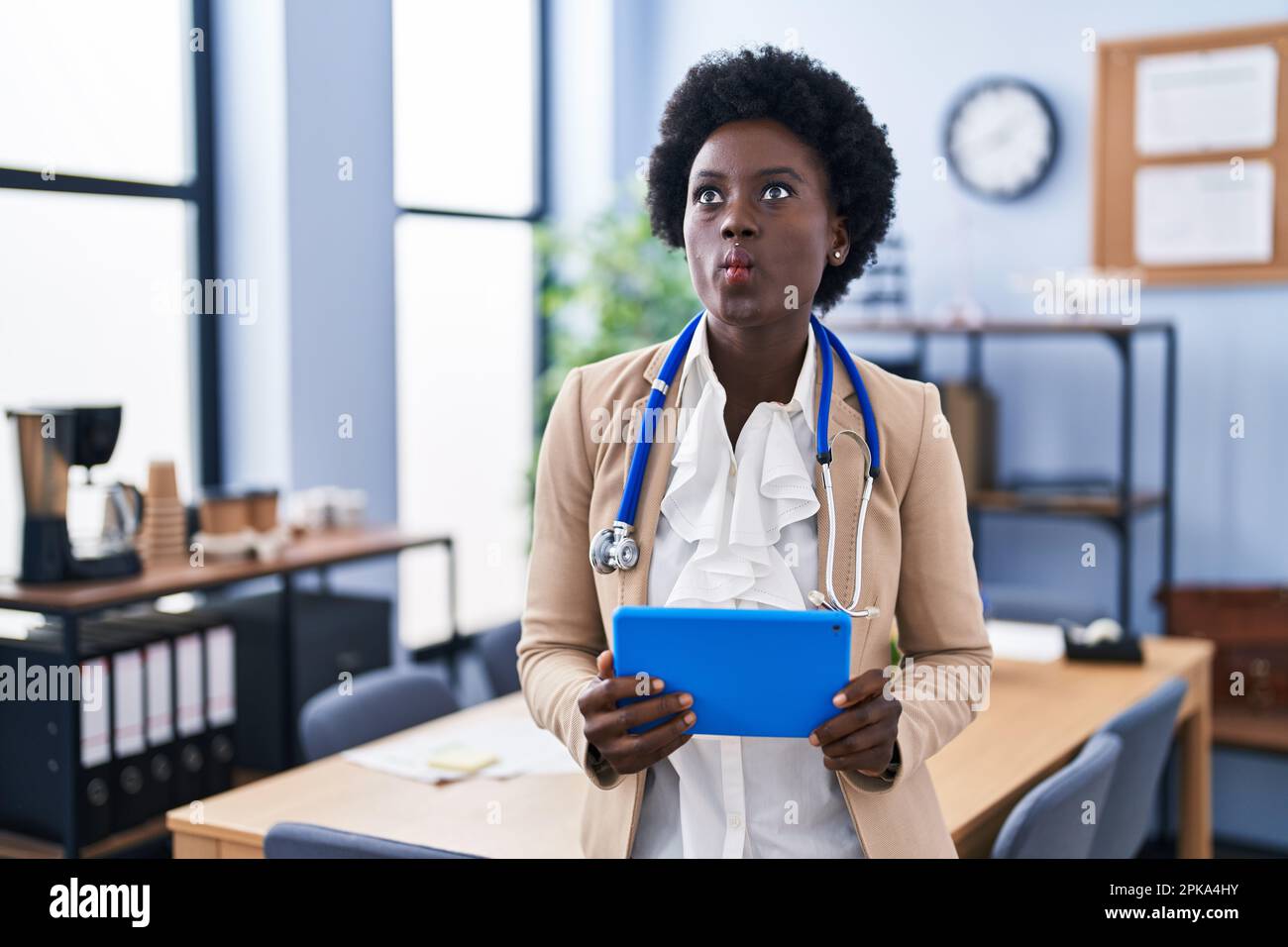 African young woman wearing doctor stethoscope making fish face with ...