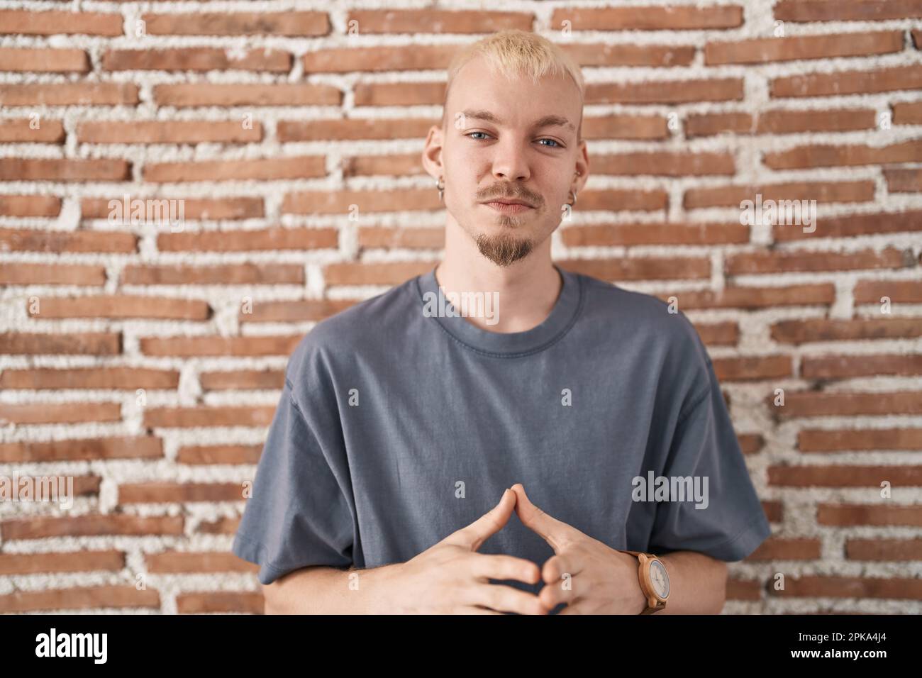 Young caucasian man standing over bricks wall hands together and ...