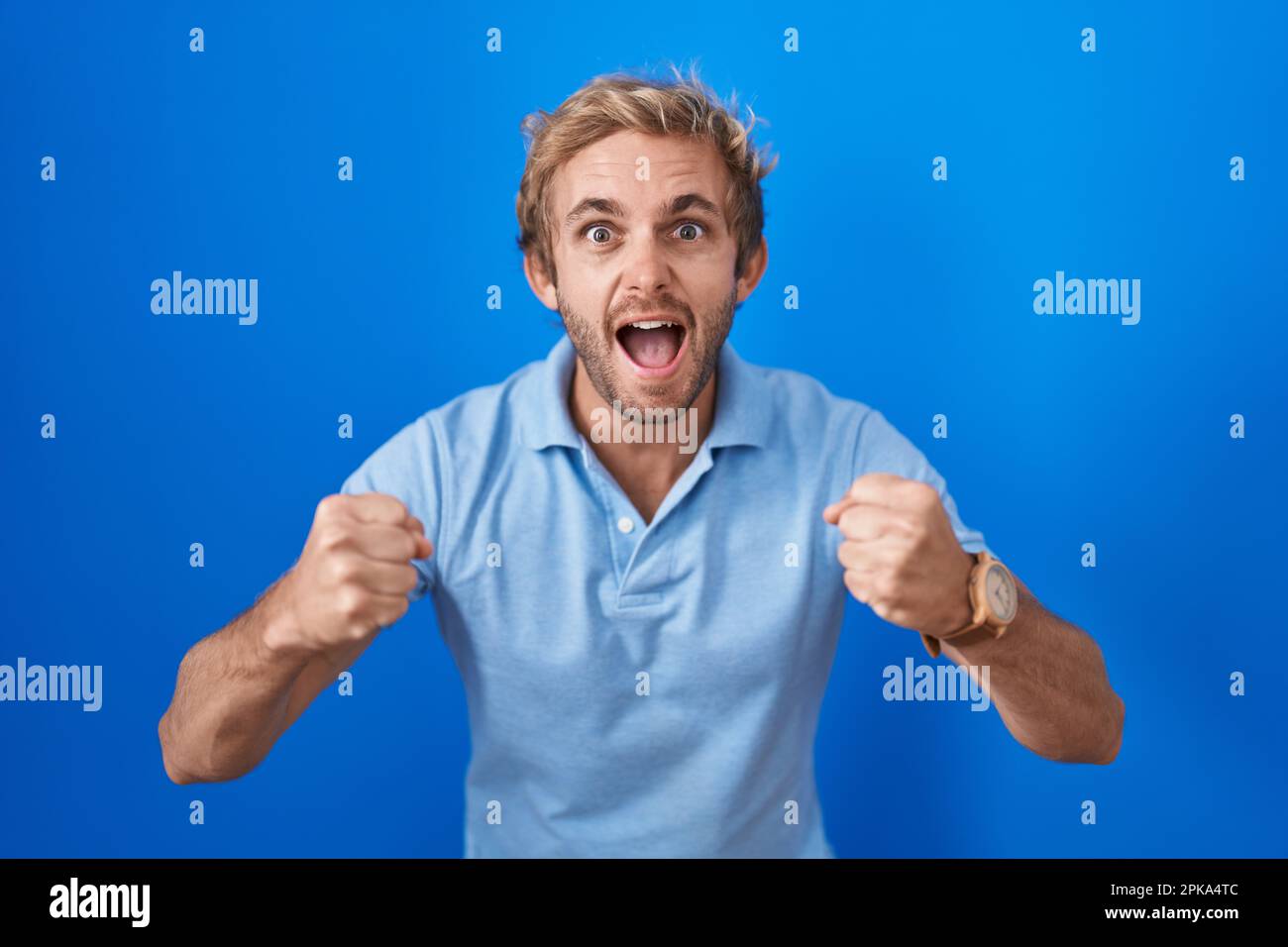 Caucasian man standing over blue background angry and mad raising fists ...