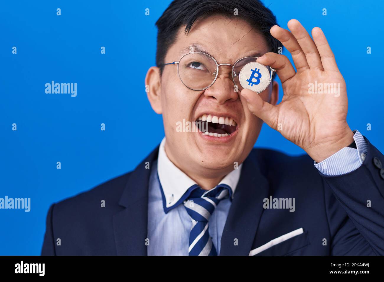 Young asian man holding virtual currency bitcoin covering eye angry and ...