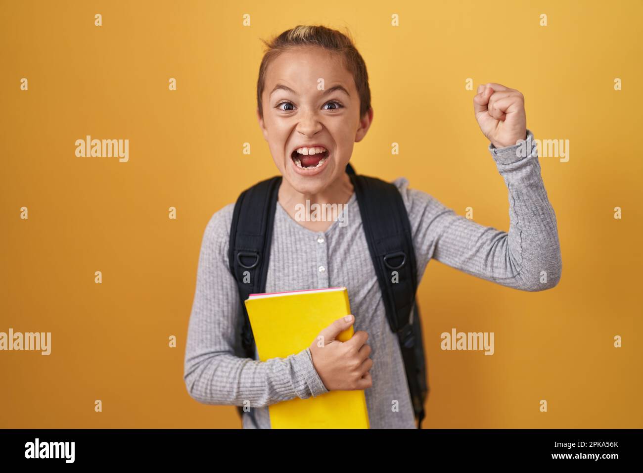 Little caucasian boy wearing student backpack and holding book annoyed ...
