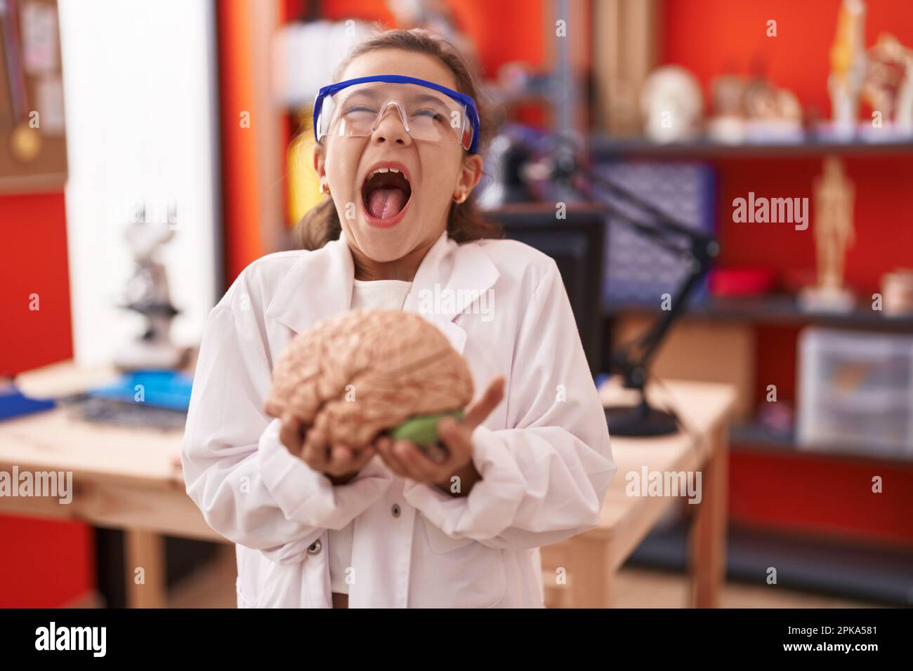 Little hispanic girl holding brain at science class at school angry and ...