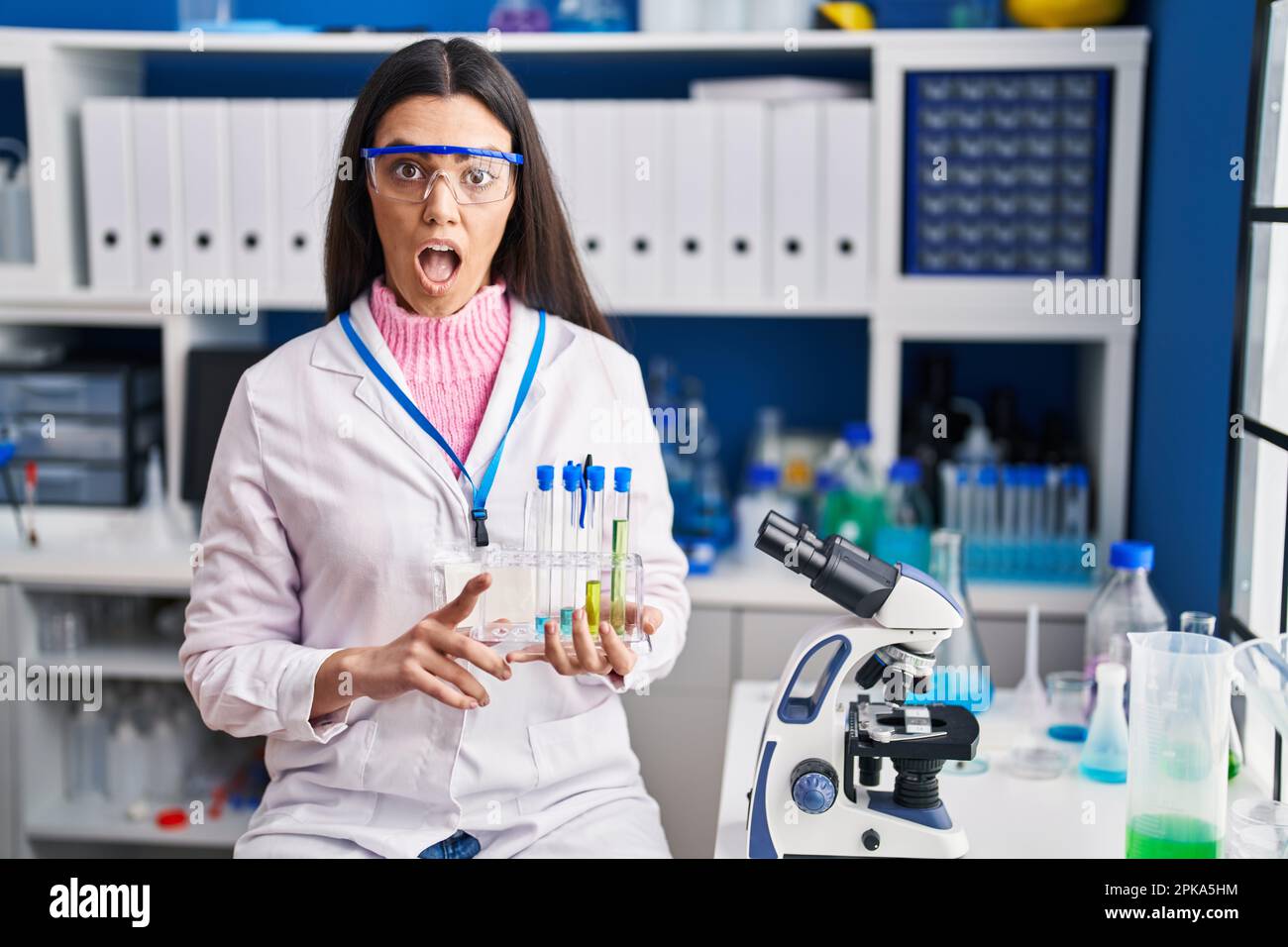 Young brunette woman working at scientist laboratory scared and amazed ...