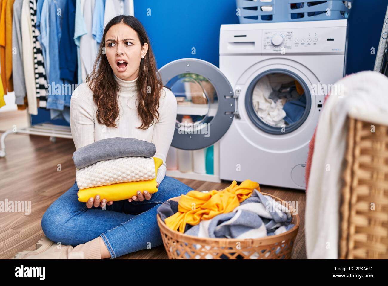 Young hispanic woman holding clean laundry angry and mad screaming frustrated and furious ...