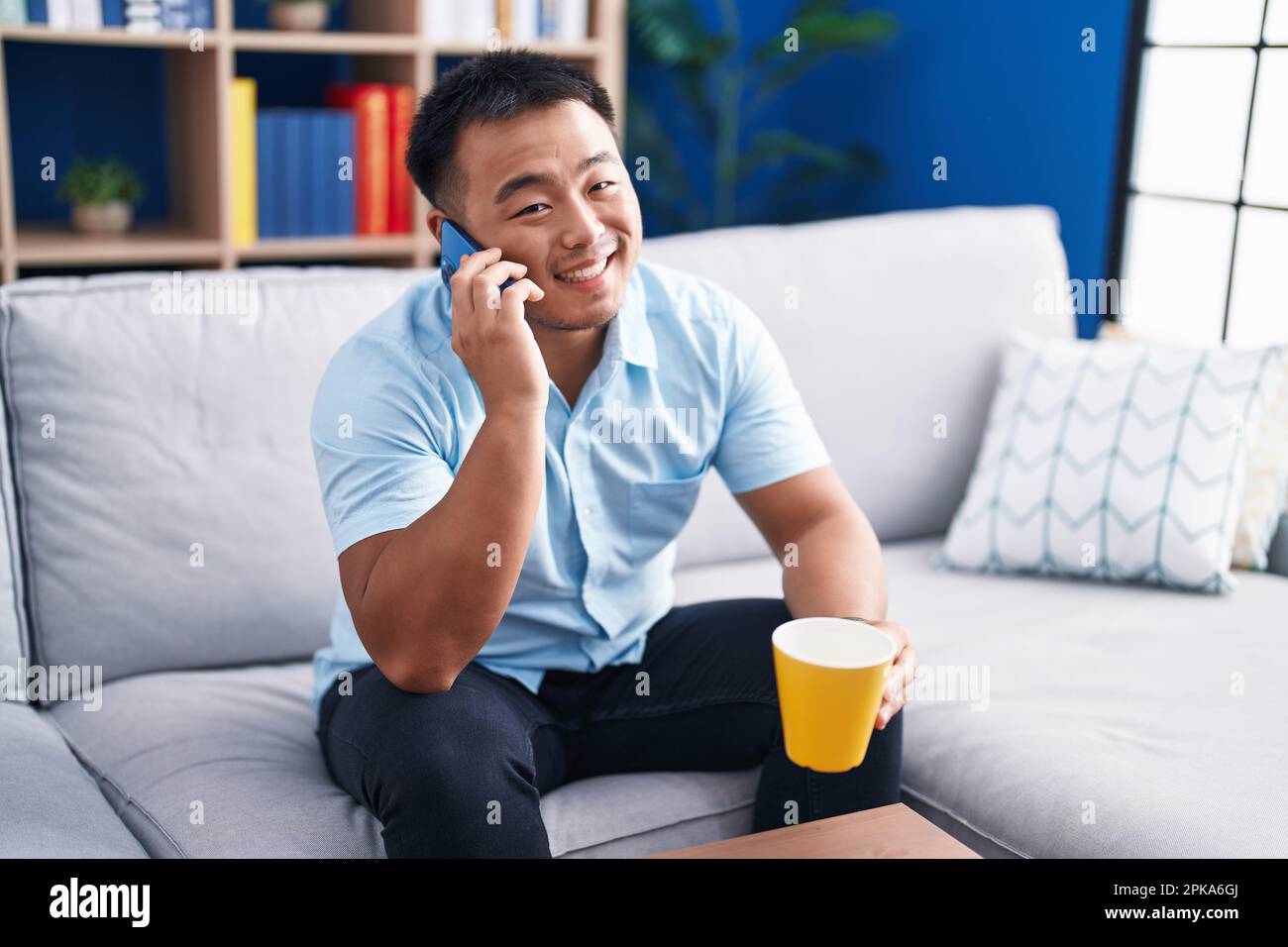 Young chinese man talking on smartphone drinking coffee at home Stock ...