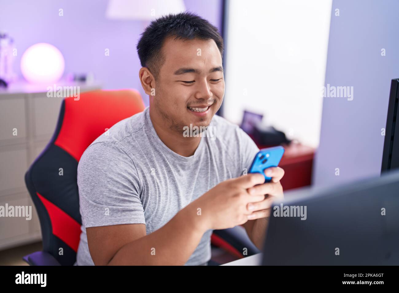 Young chinese man streamer using computer and smartphone at gaming room ...