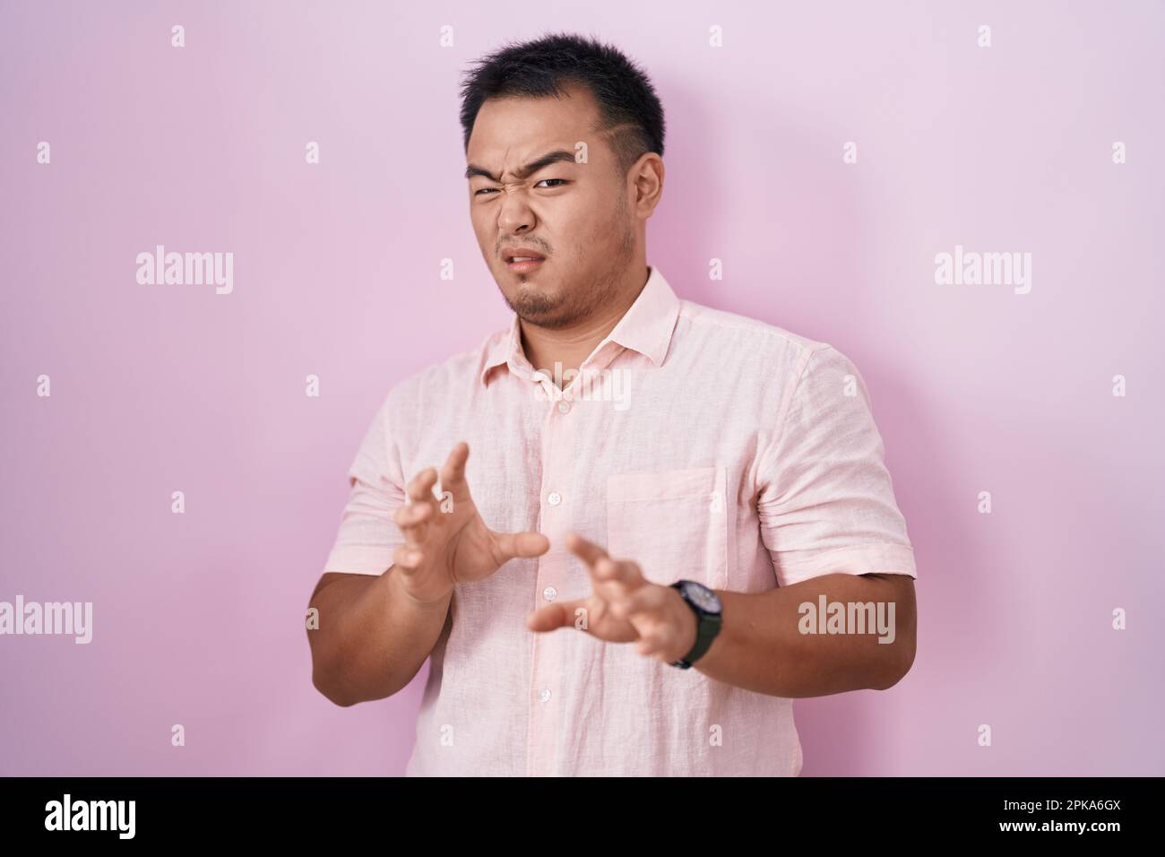 Chinese young man standing over pink background disgusted expression ...