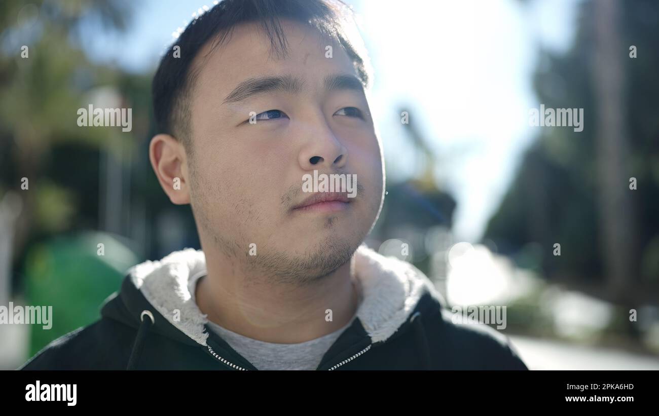 Young chinese man looking to the side with serious expression at street ...