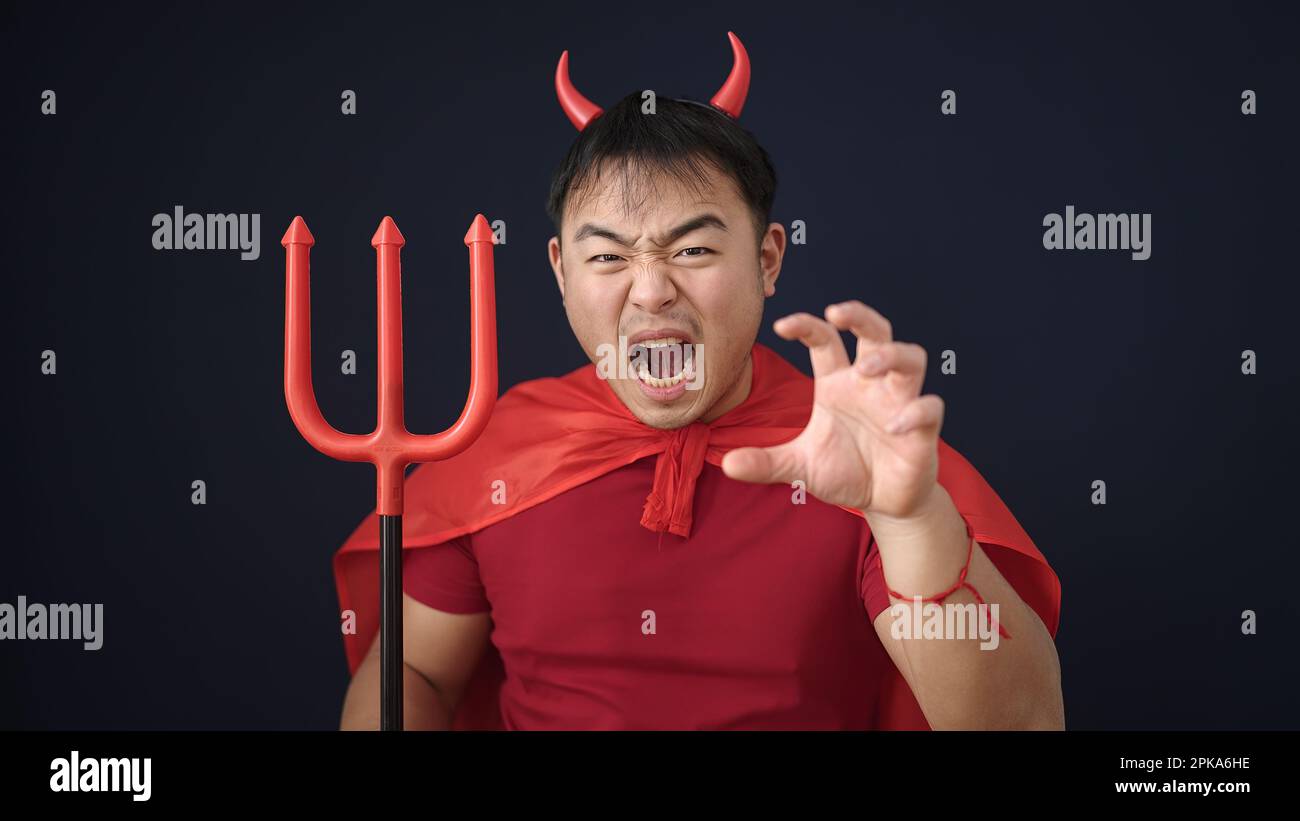 Young chinese man wearing devil costume doing scare gesture over ...
