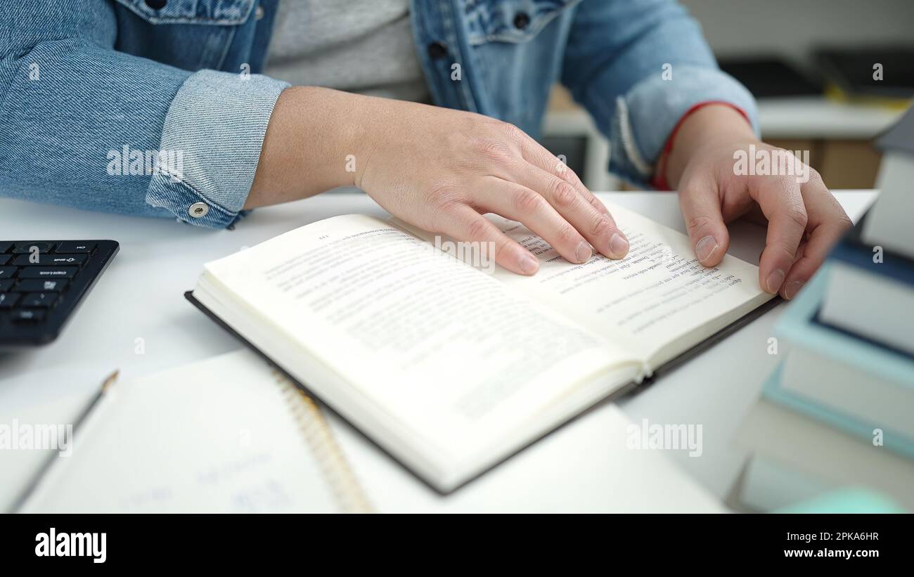 Young chinese man student reading book sitting on table at library ...