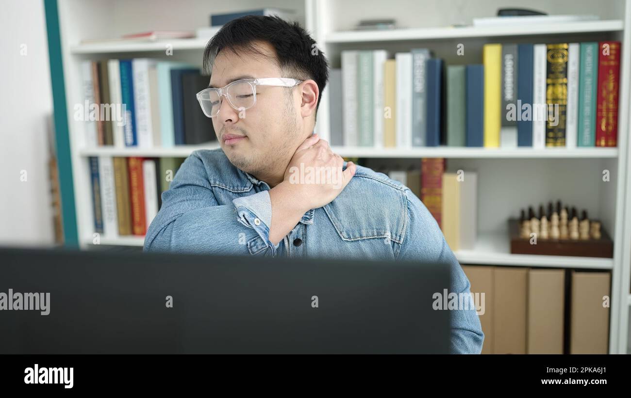 Young chinese man student using computer stressed at library university ...