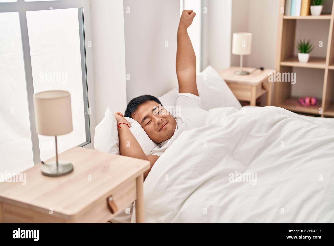 Young chinese man stretching arms lying on bed at bedroom Stock Photo ...