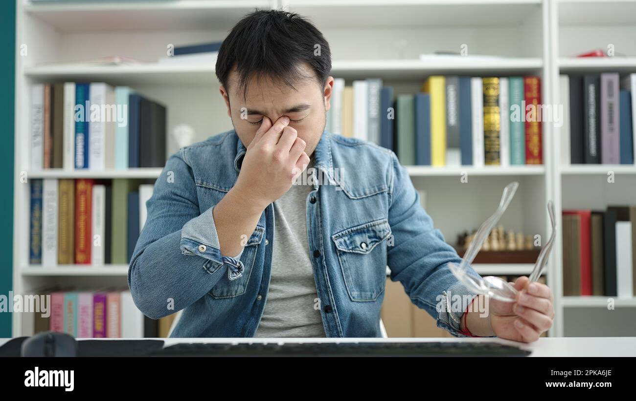 Young chinese man student using computer stressed at library university ...