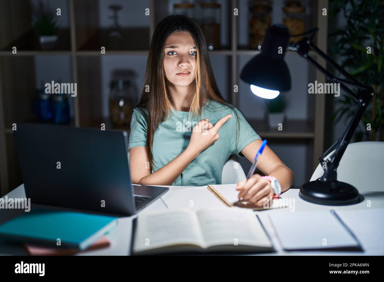 Teenager girl doing homework at home late at night pointing aside ...