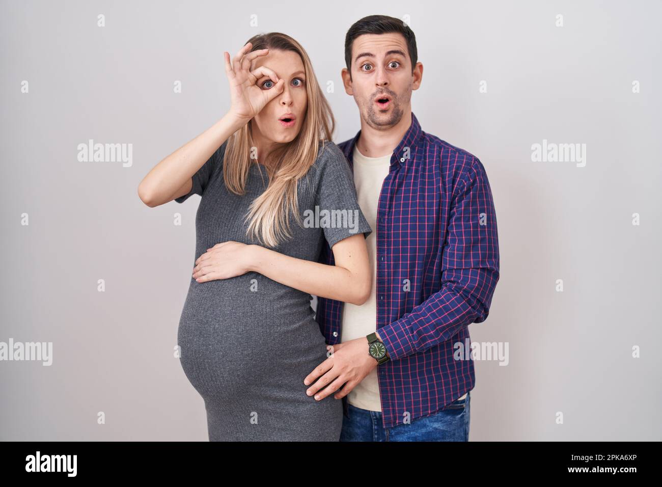 Young couple expecting a baby standing over white background doing ok ...