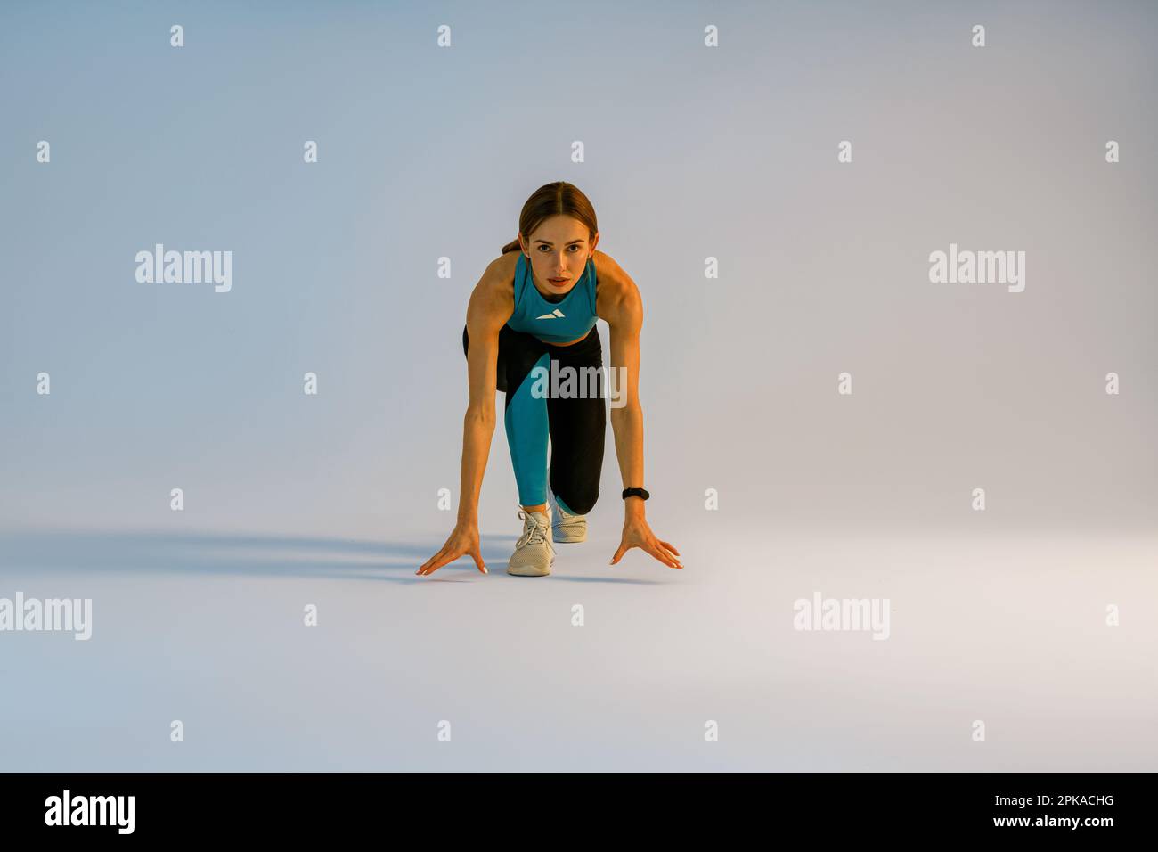 Female athlete in starting position ready for running looking at camera ...