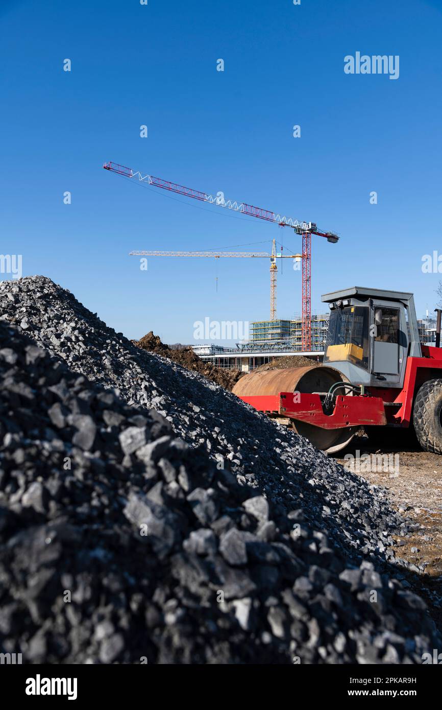 Red roller stands on large construction site in front of gravel mounds ...
