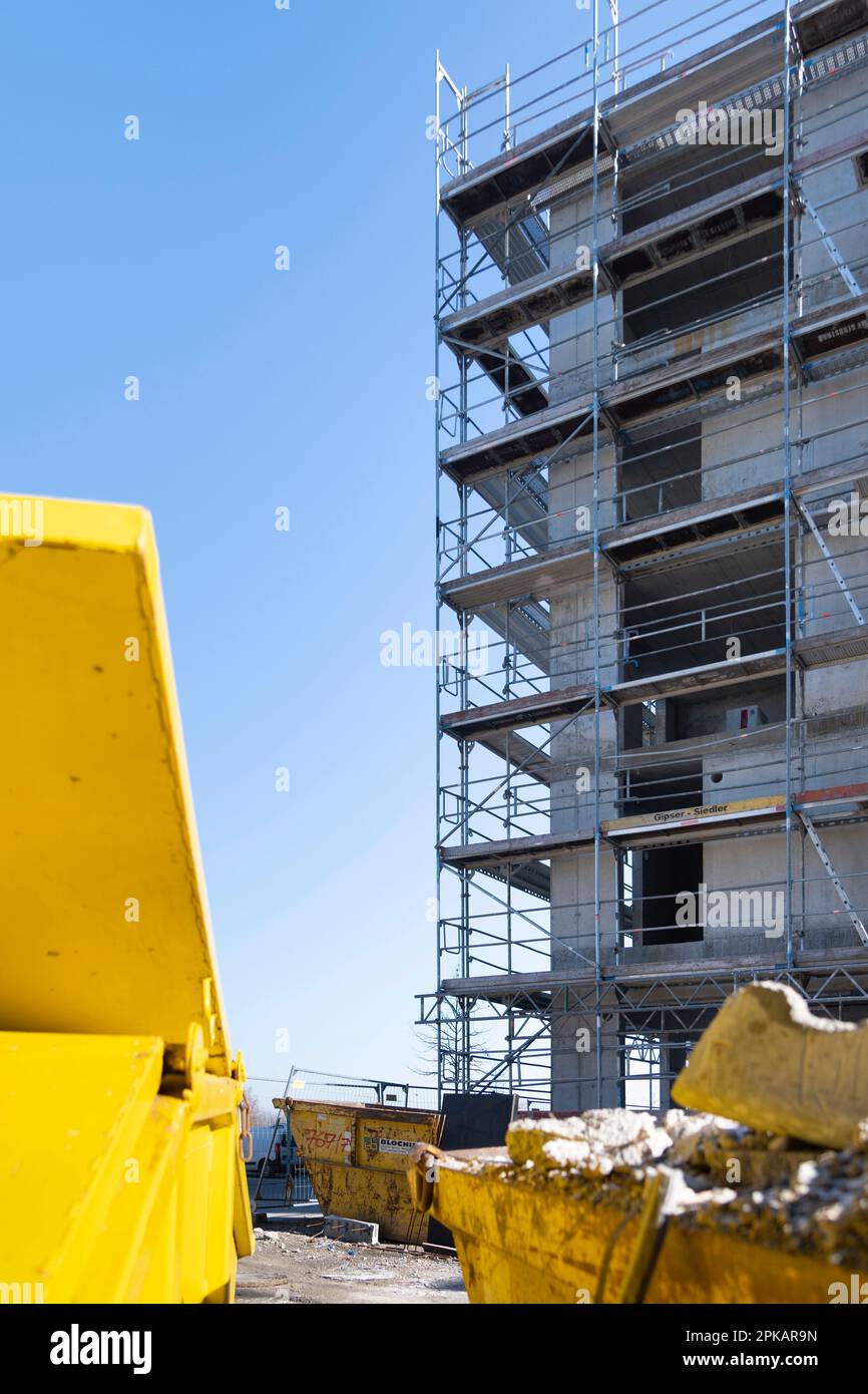 Yellow container for construction waste stands in front of scaffolded ...