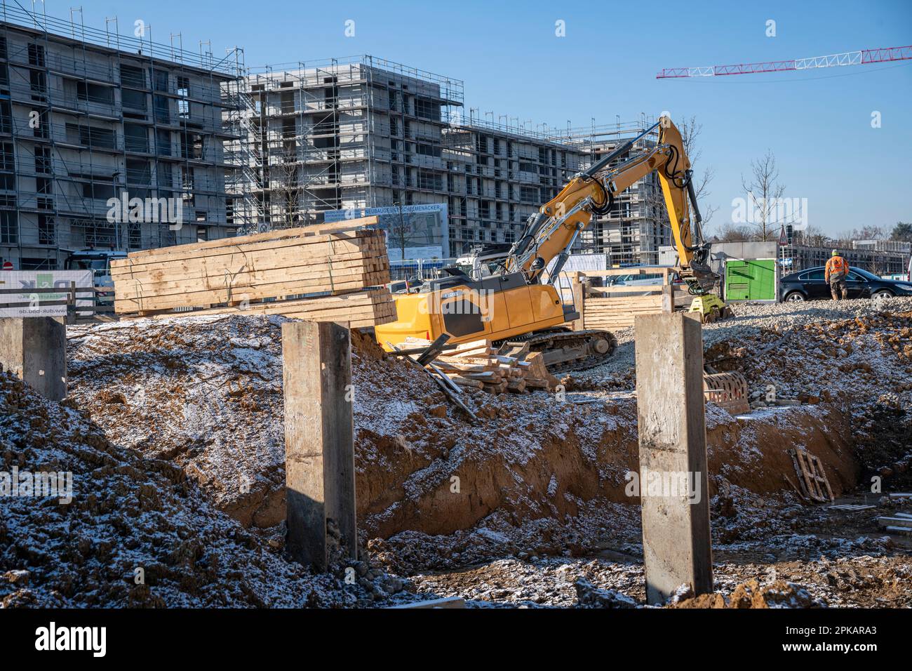 On a large construction site in winter, a yellow excavator digs a ...