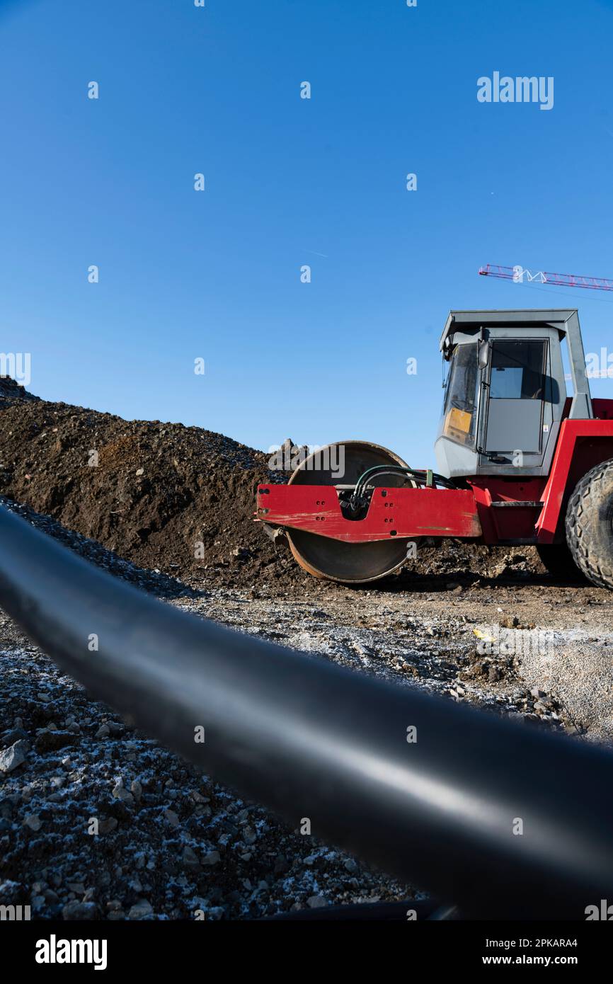 Red roller stands on large construction site in front of pile of ...