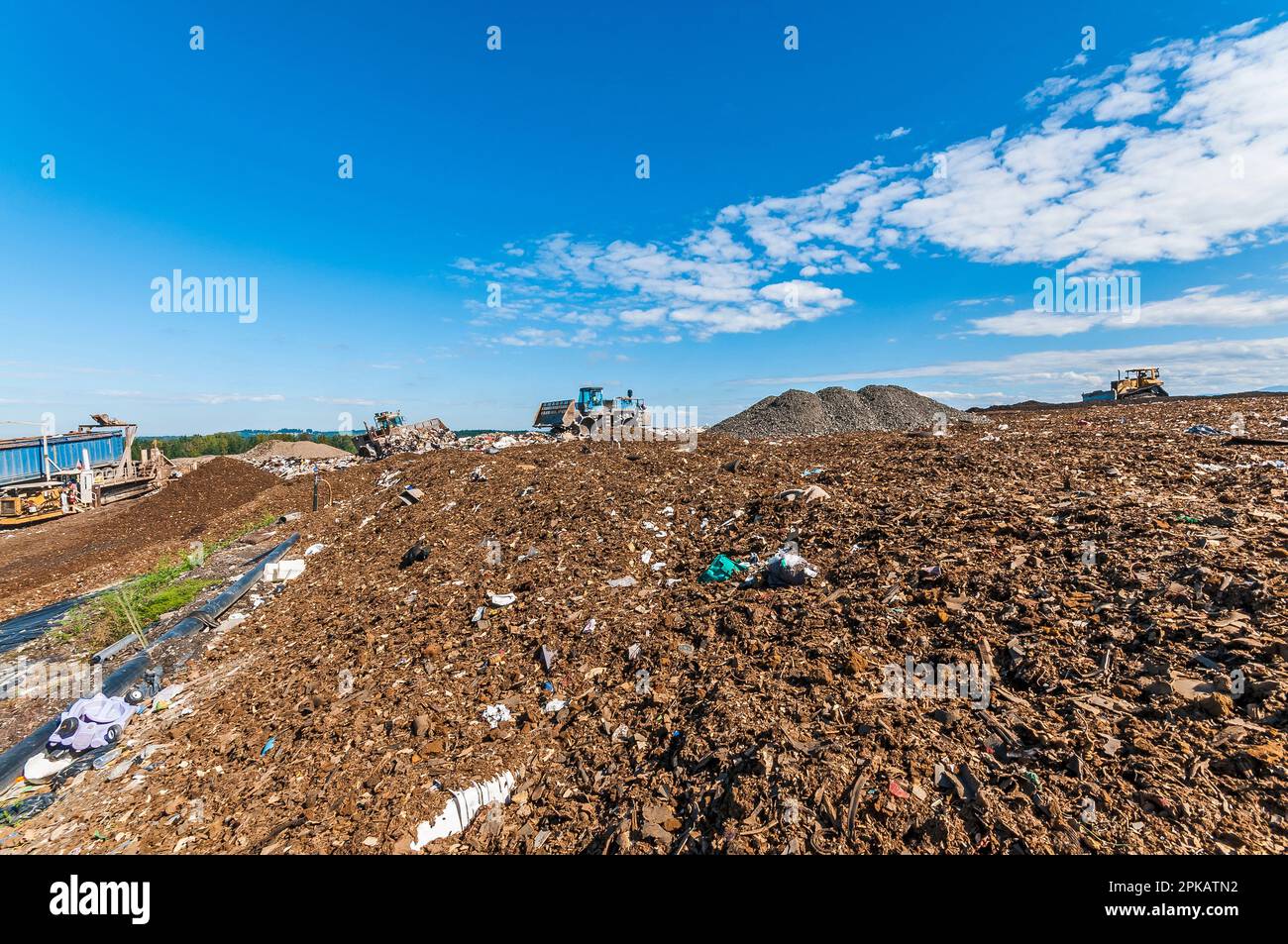 Soil compactors moving around and manipulating trash in the dirt on a ...