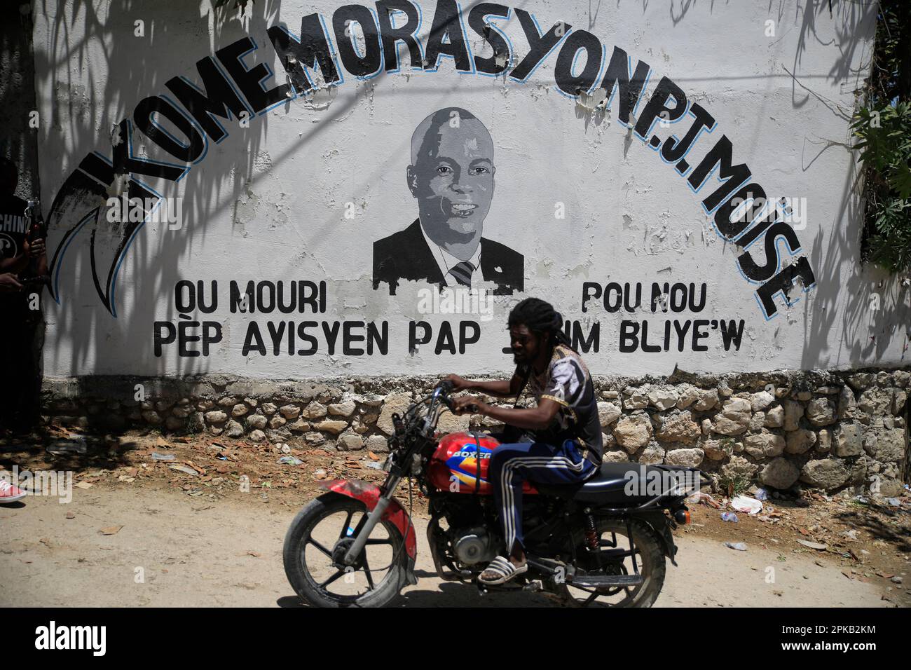 A moto-taxi driver rides past a mural featuring slain Haitian President ...