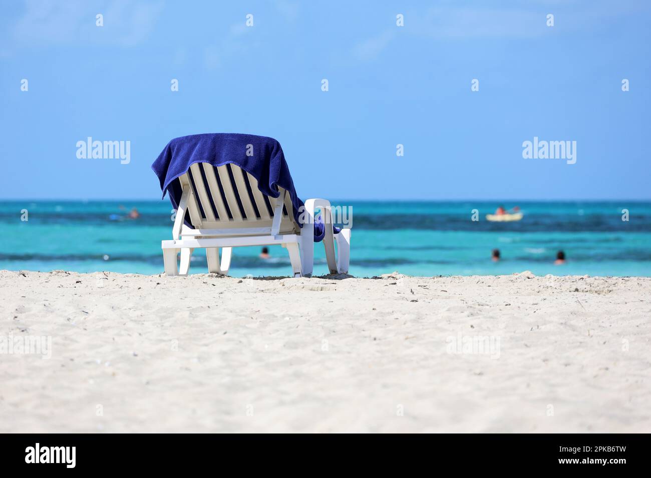 Deck chair with blue towel on sandy beach on swimming people background ...