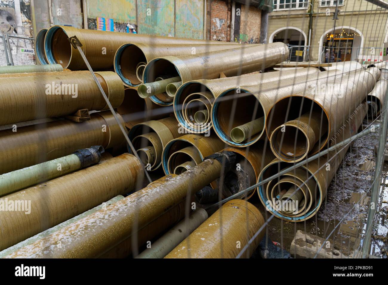 Pipelines of different diameters lie behind a fence on a city street ...