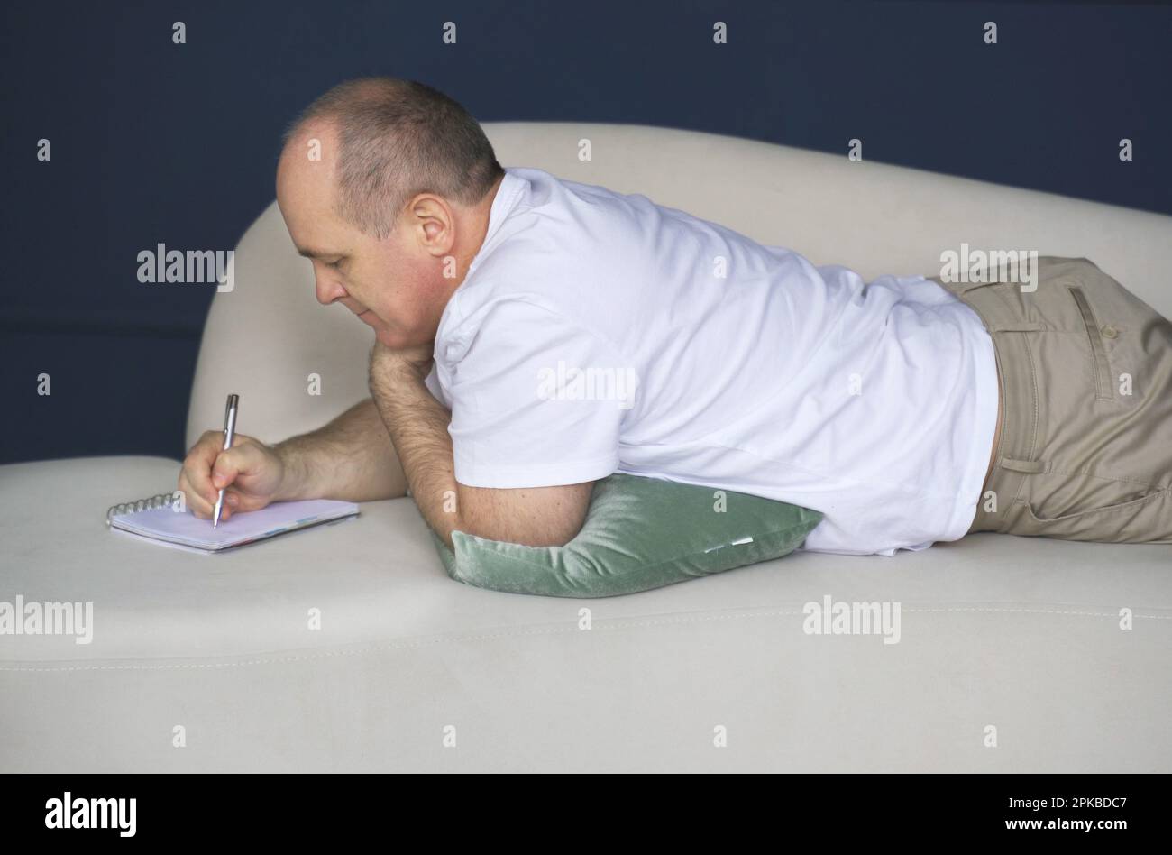 Young man lying on sofa and writing to do list in notepad Stock Photo ...