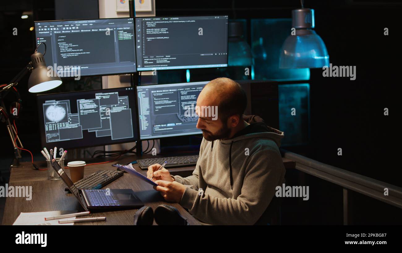 It System Engineer Comparing Data Files On Clipboard Papers And Multiple Monitors To Program New