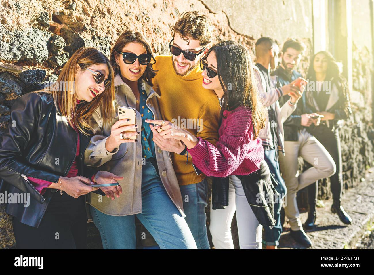 Four friends laugh at smartphone content in front of old wall in ...