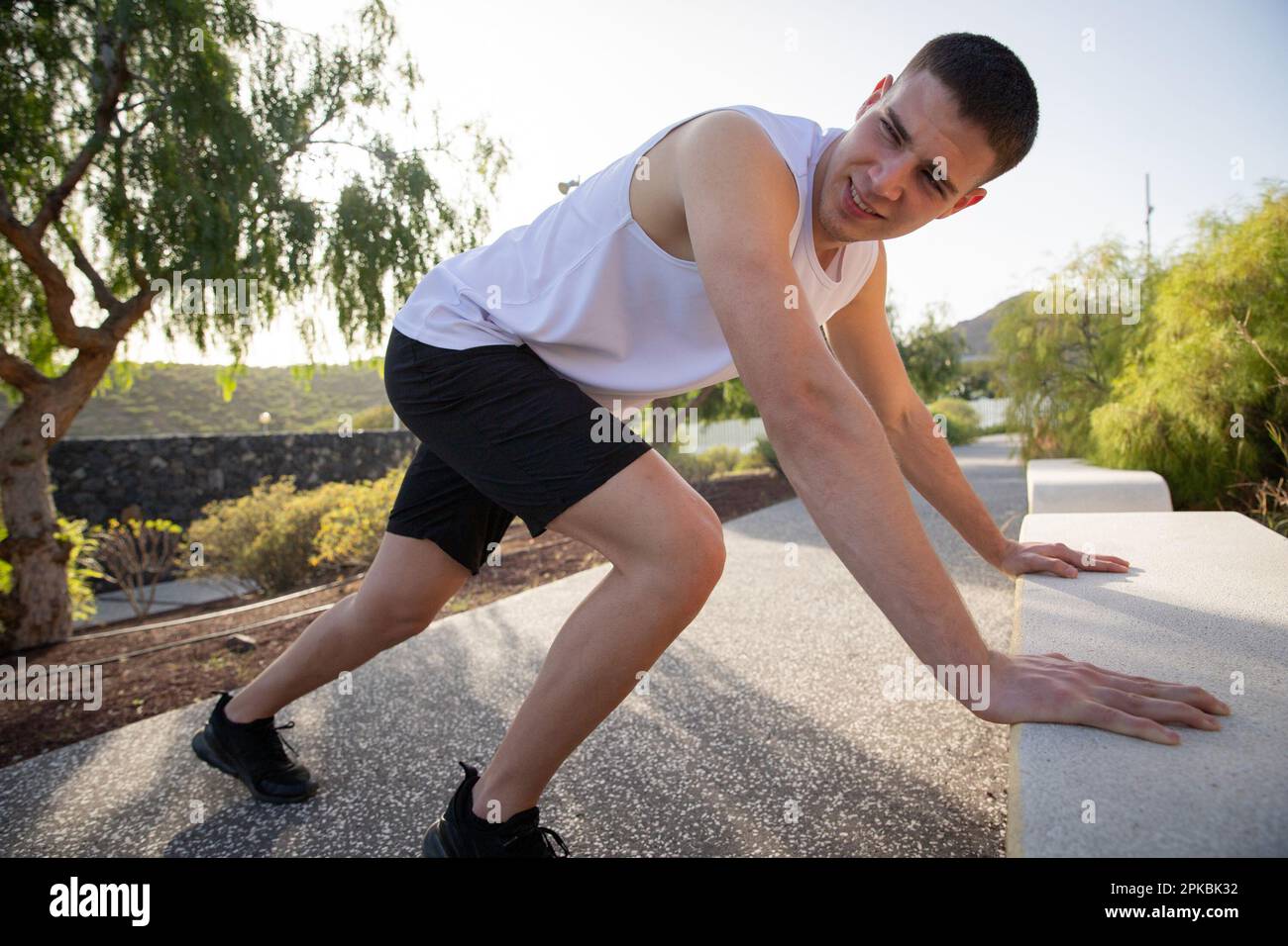 A young athlete performs stretching exercises with a bench in an open ...