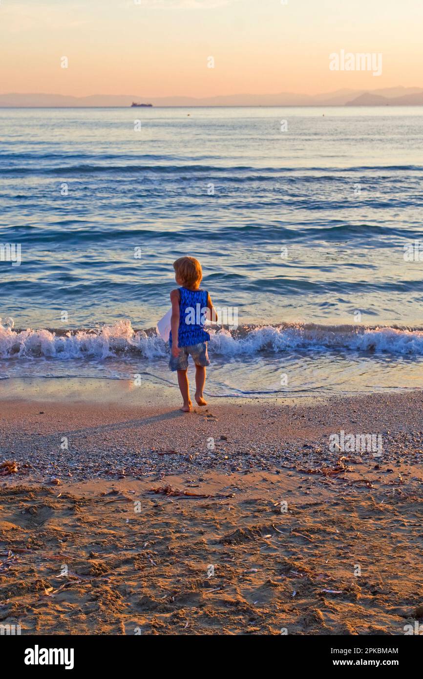 little boy on the beach with sand goes to the sea at sunset Stock Photo ...