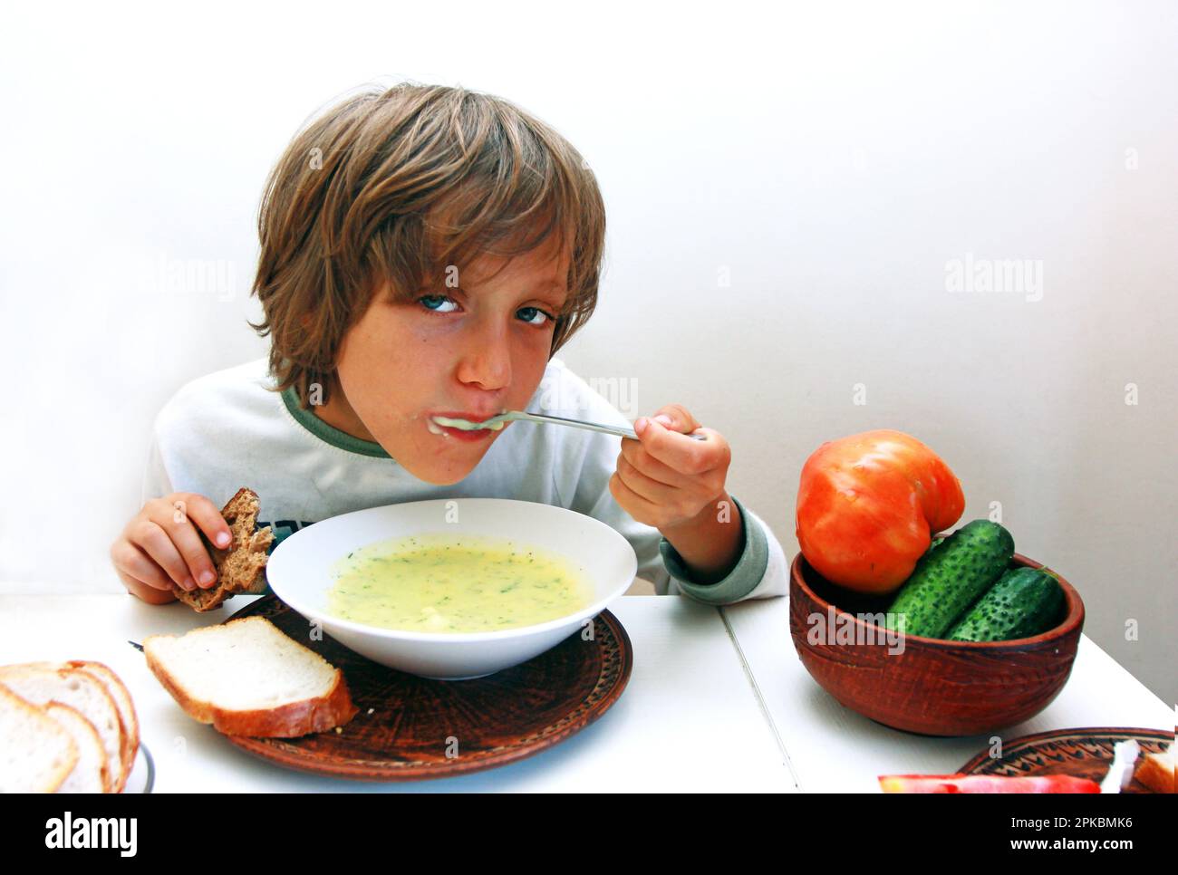 boy eats vegetable soup with spoon and bread at the dinner table Stock ...