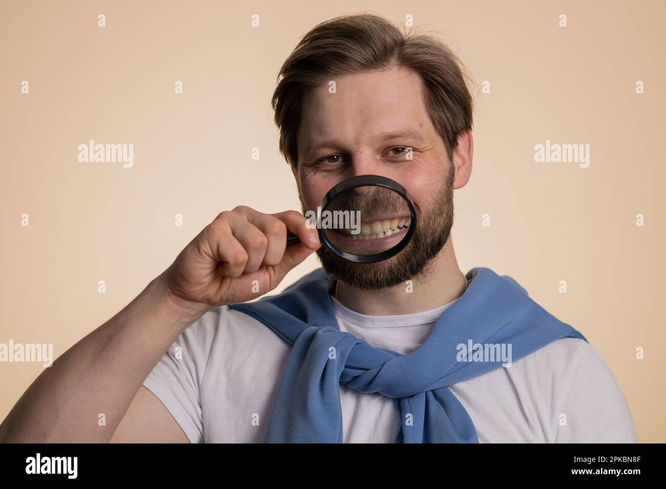 Caucasian man holding magnifier glass on healthy white teeth, looking ...