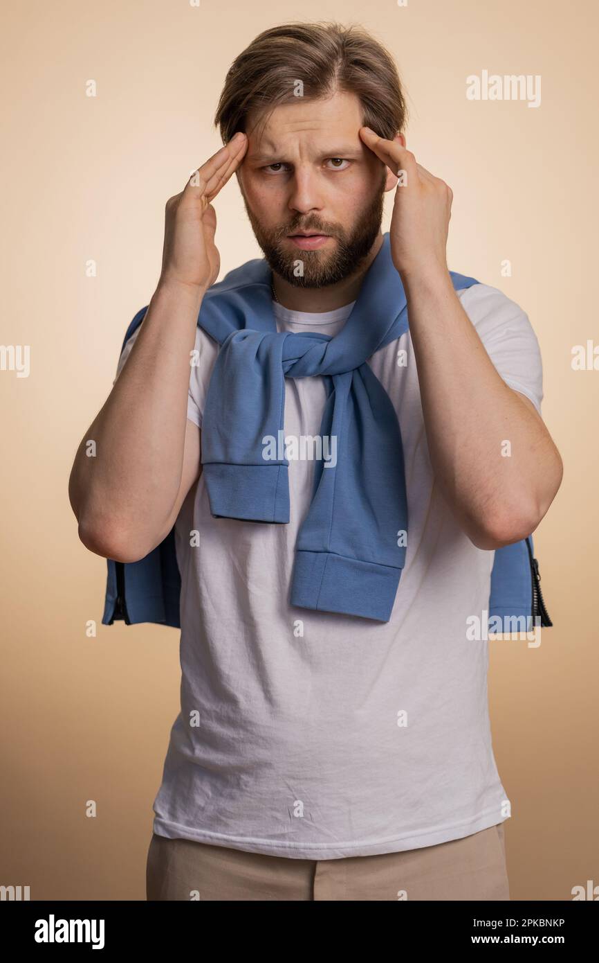 Sick ill caucasian bearded young man rubbing temples to cure headache ...