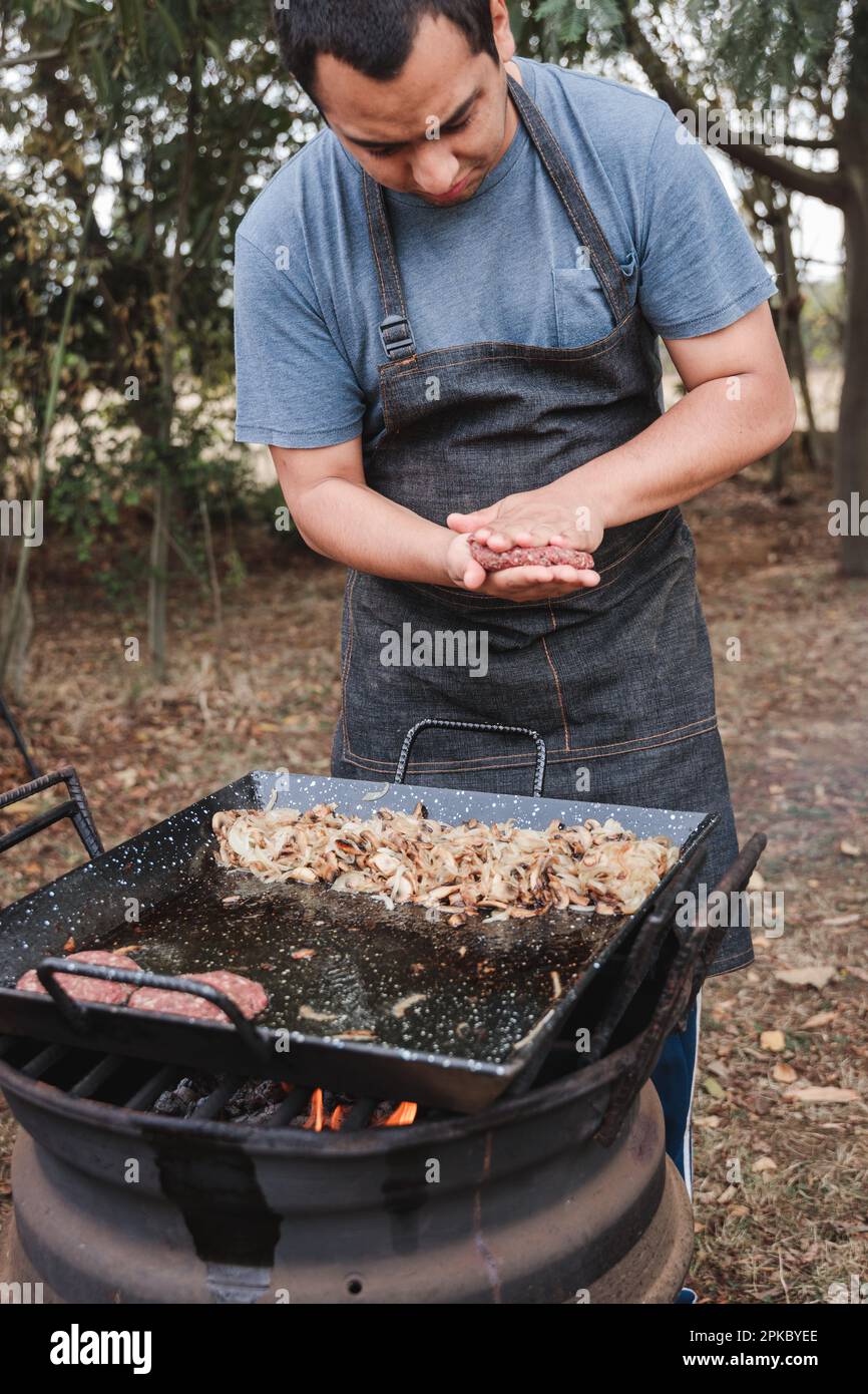 Young latin man cooking homemade hamburgers and onion on a barbecue ...
