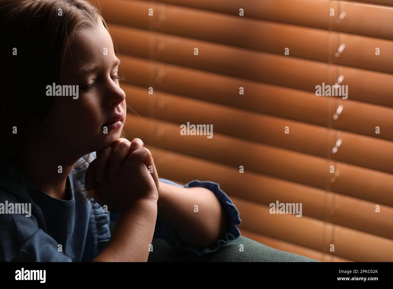 Cute little girl praying near window. Space for text Stock Photo - Alamy