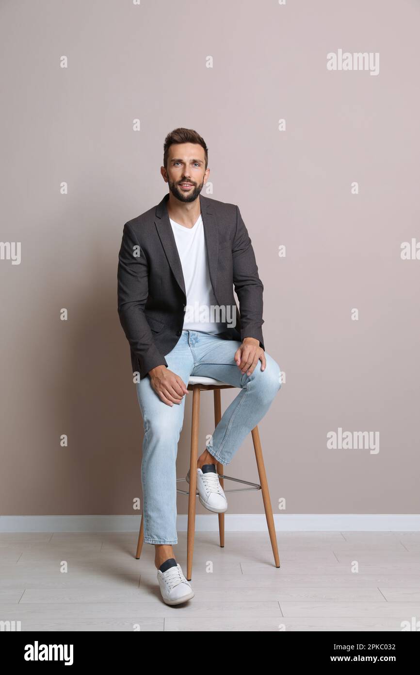 Handsome man sitting on stool near beige wall Stock Photo - Alamy