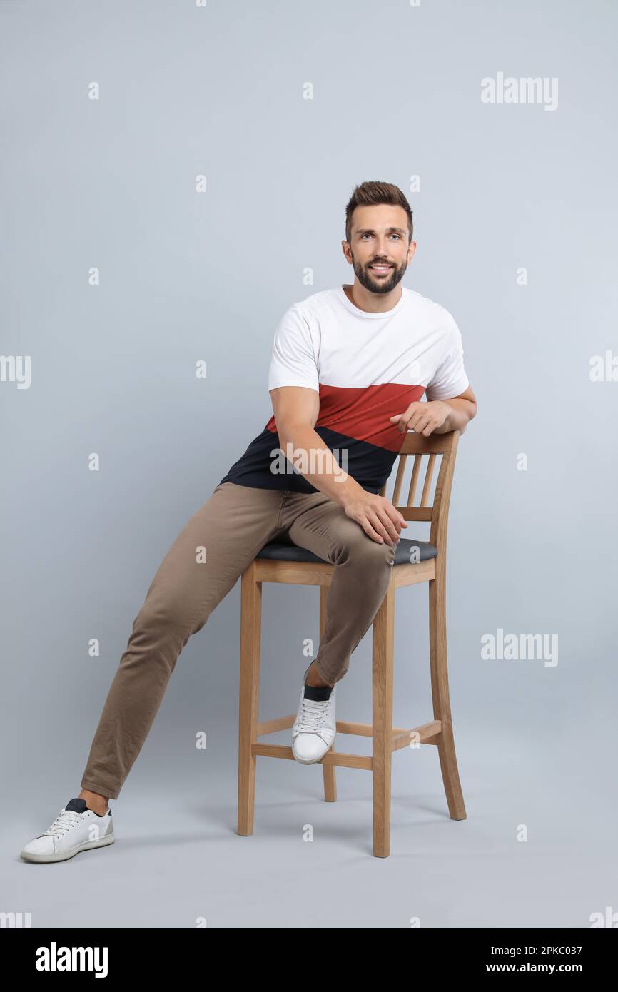 Handsome man sitting on stool against light grey background Stock Photo ...